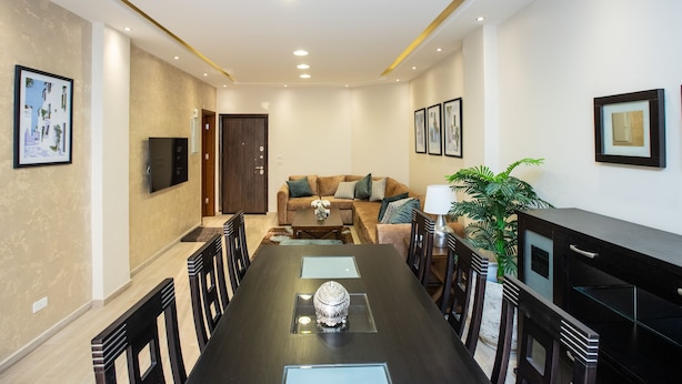 Uma sala de jantar moderna com uma mesa comprida, cadeiras, um sofá e uma televisão.