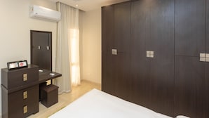 Quarto de hotel com cama, escrivaninha com gavetas, guarda-roupa e ar condicionado.