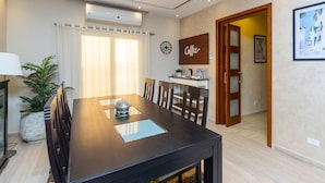 Uma área de refeições com uma mesa de madeira escura, cadeiras, um vaso de planta e um letreiro de café na parede.