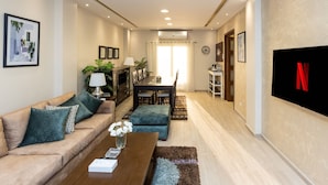 Uma sala de estar moderna com sofá, mesa de centro e televisão. Há também uma área de jantar com mesa e cadeiras.
