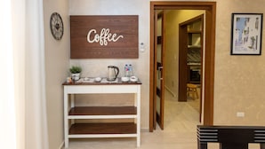 Uma cozinha com um letreiro de café, chaleira e uma pequena mesa com xícaras e um vaso de planta.