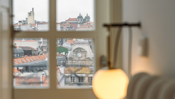 Janela com vista para um horizonte urbano, incluindo um campanário e diversos edifícios.