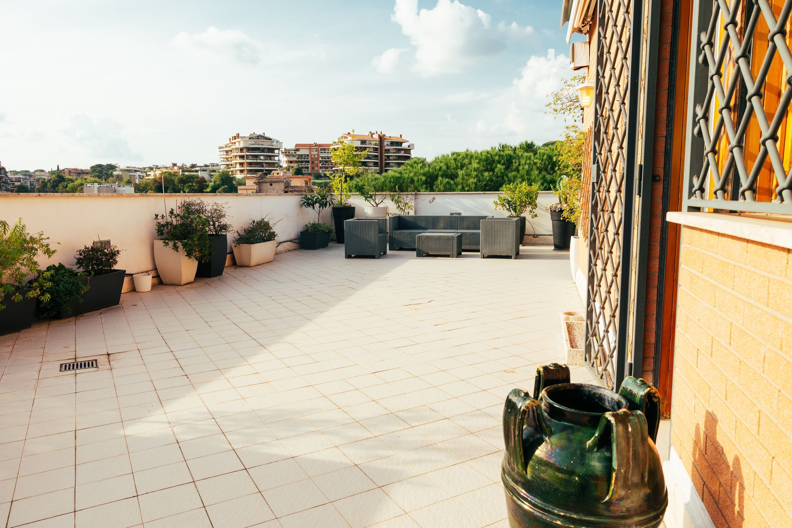 Terraço no telhado com piso de azulejos, mobiliário de exterior, plantas em vasos e vista dos edifícios circundantes.