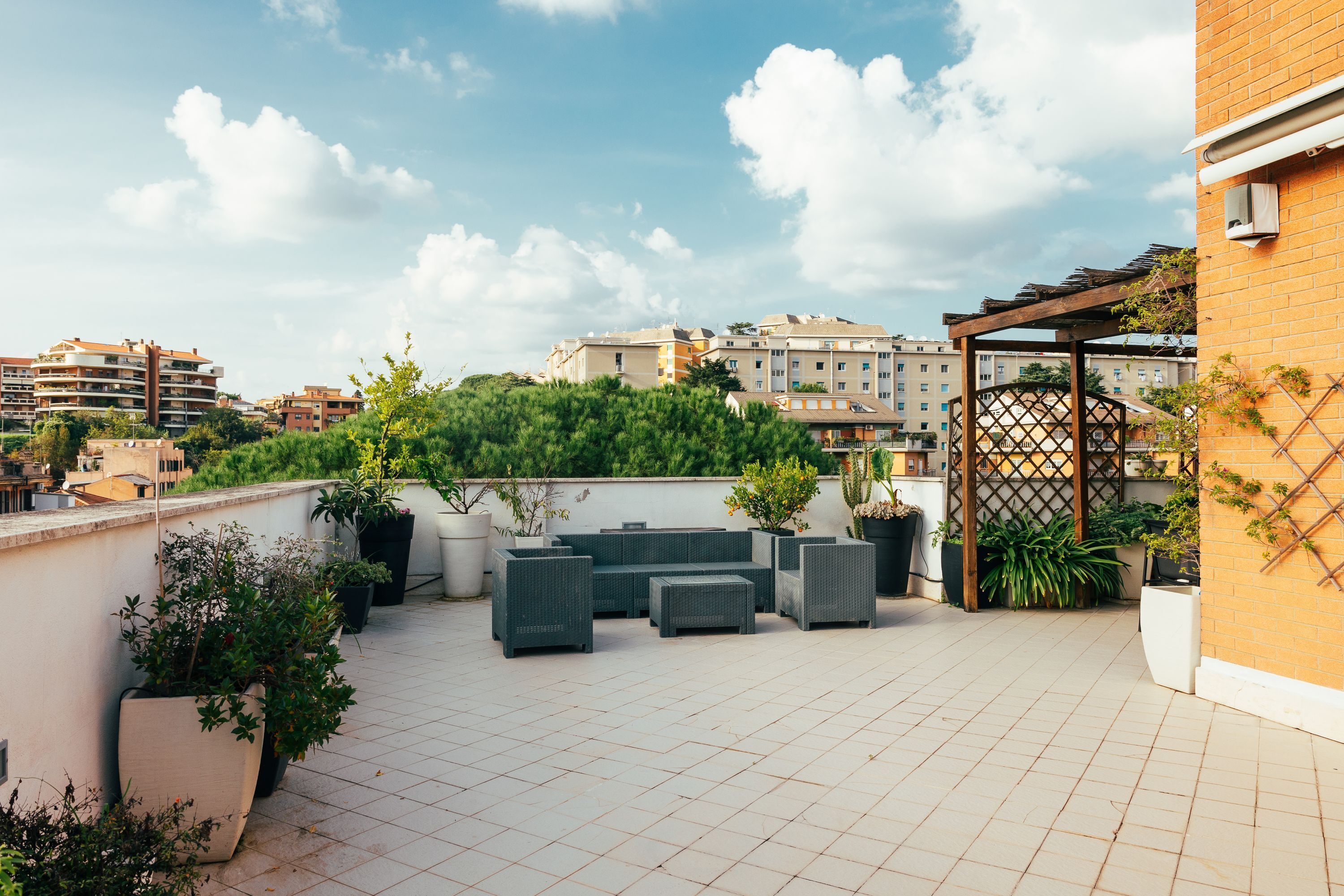 Terraço no terraço com móveis de exterior, plantas em vasos e vista para edifícios circundantes.