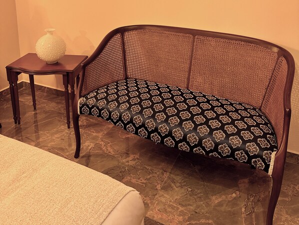 Uma cama com cabeceira e peseira estampadas, uma pequena mesa com um vaso, e piso coberto por carpete.