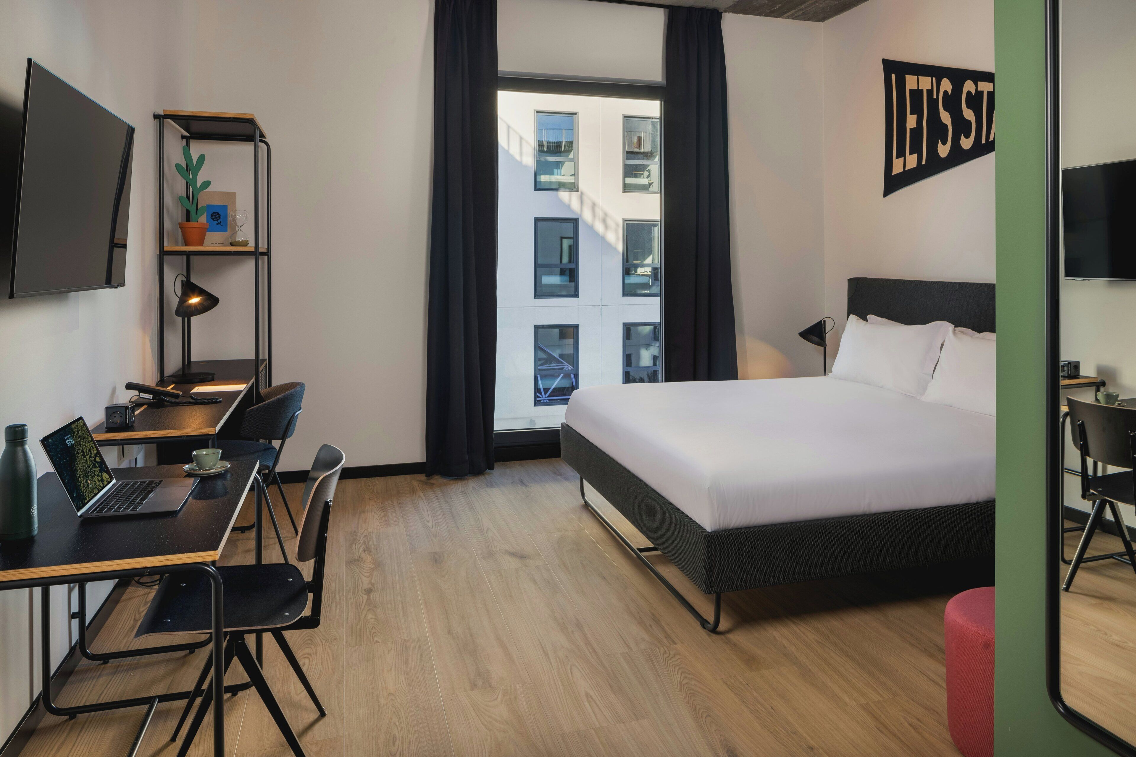 Quarto de hotel moderno com cama, escrivaninha, cadeira, TV e janela com vista para edifícios.
