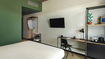 Quarto de hotel com cama, secretária com cadeira, televisão e guarda-roupa.