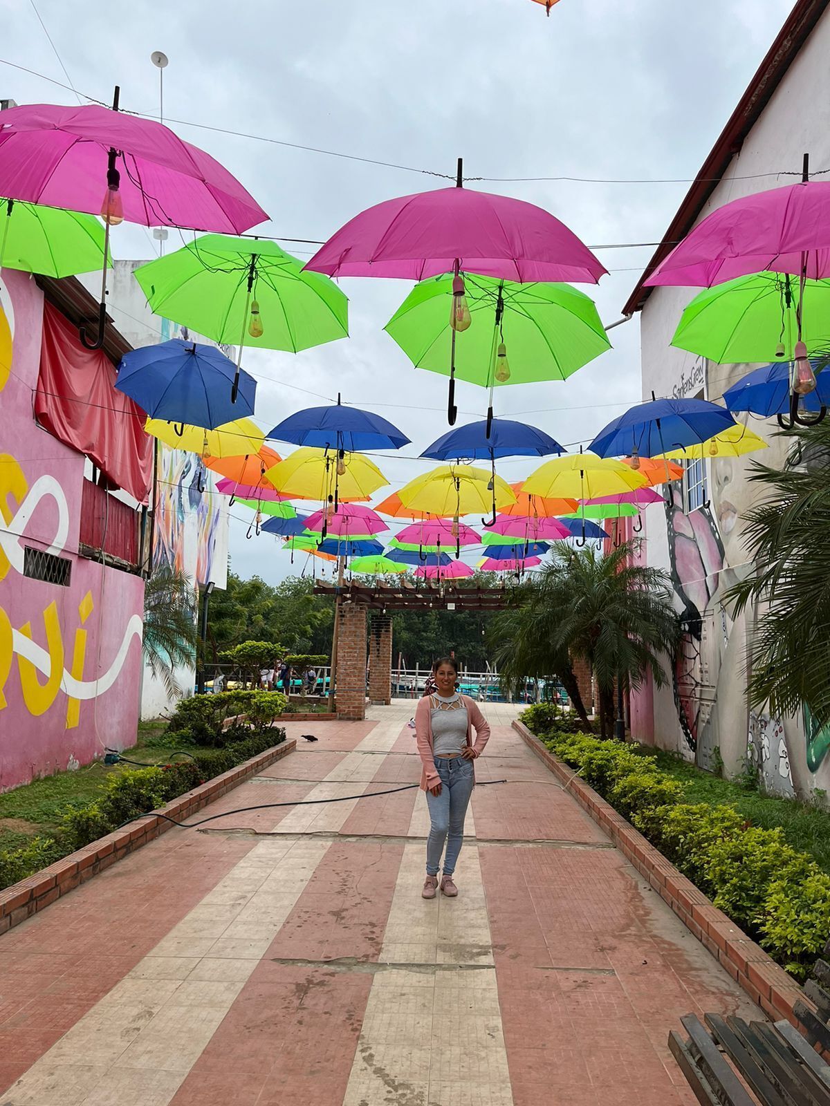 Uma passagem com guarda-sóis coloridos acima e um mural no prédio à esquerda.
