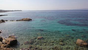 Vista costeira com águas turquesa transparentes, margem rochosa e terra ao longe.
