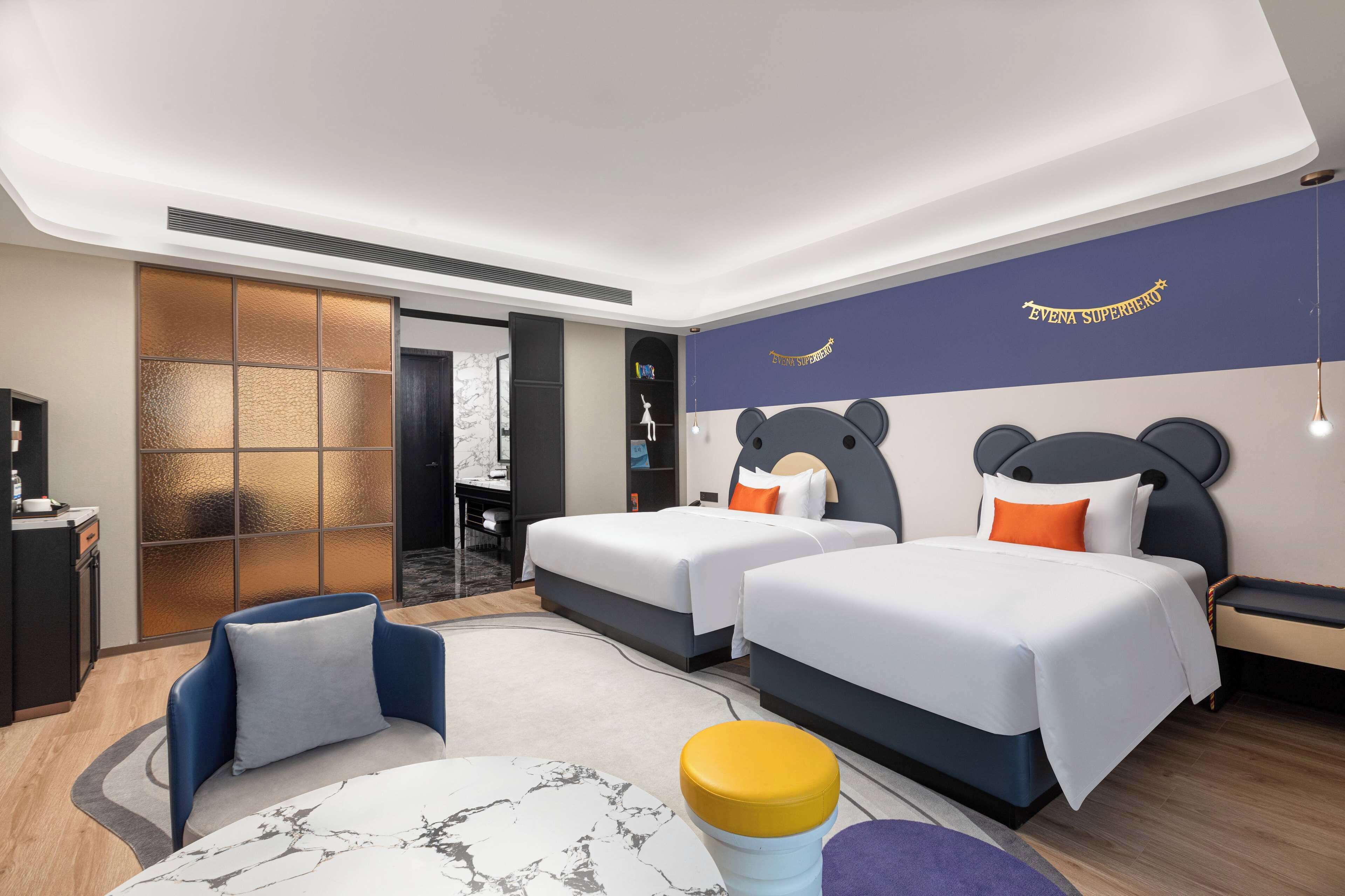 Quarto de hotel moderno com duas camas, uma escrivaninha, uma cadeira e um sofá.