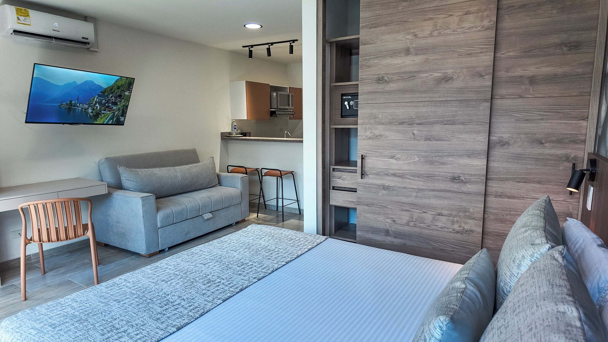 Quarto de hotel moderno com cama, sofá, escrivaninha e televisão.
