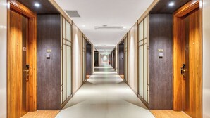 Um corredor de hotel com portas de madeira e chão de azulejos, que dá acesso a vários quartos.