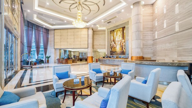 Um hall amplo com teto alto, um candelabro, área de estar com mesas redondas e um balcão de recepção.