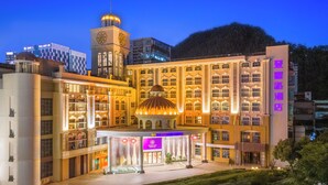Um hotel com uma estrutura central em cúpula, diversas janelas e uma torre do relógio.