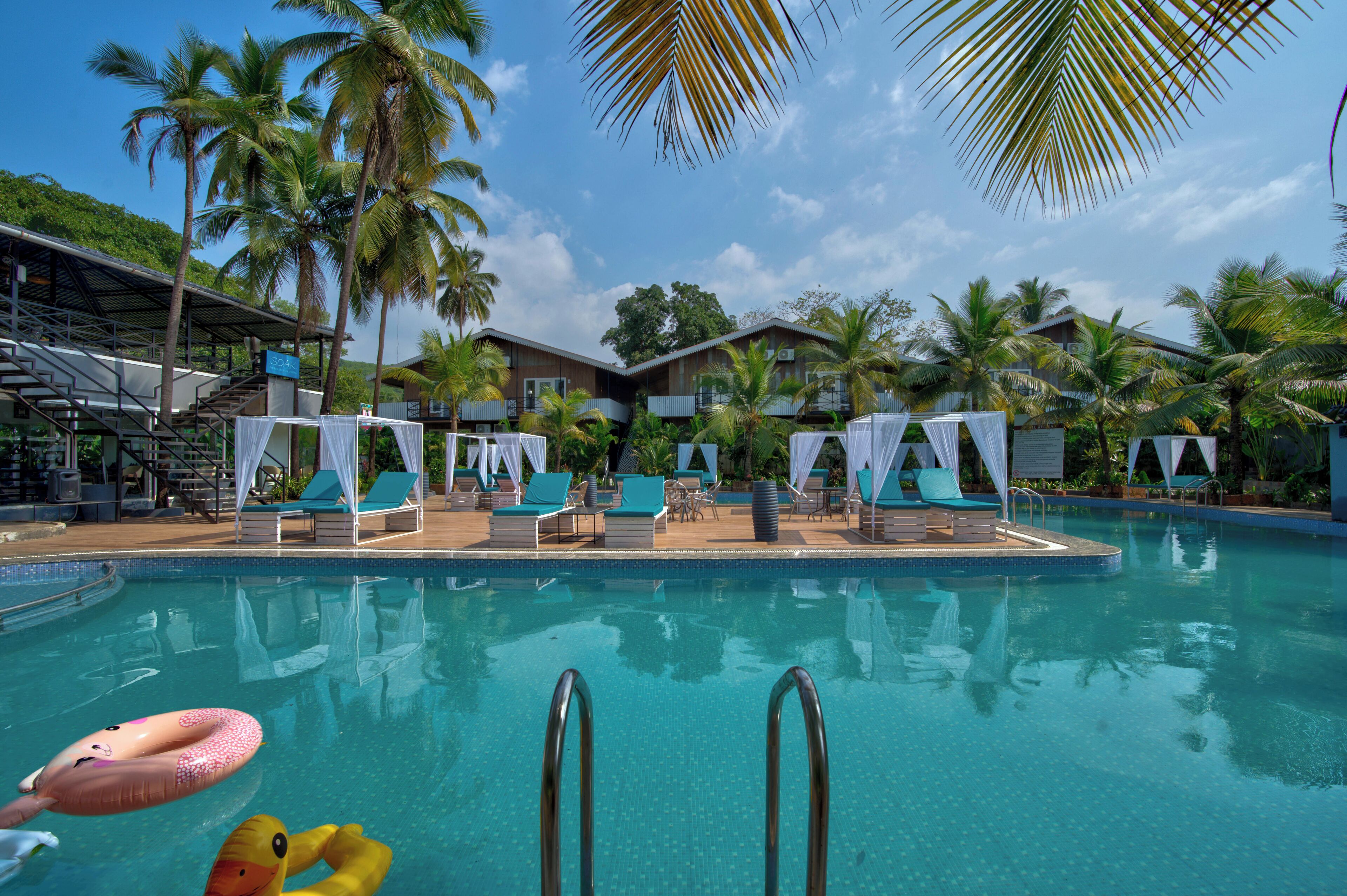 Área de piscina com espreguiçadeiras, guarda-sóis e palmeiras.