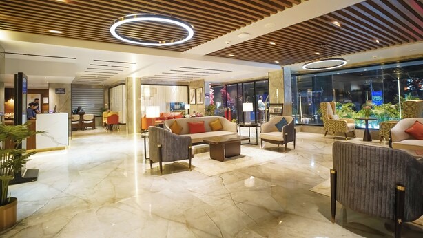 Um saguão de hotel moderno com balcão de recepção, área de estar e vista para a cidade através de grandes janelas.
