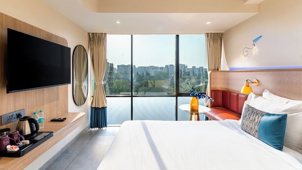 Quarto de hotel moderno com uma cama grande, televisão de tela plana, sofá e vista para a cidade.