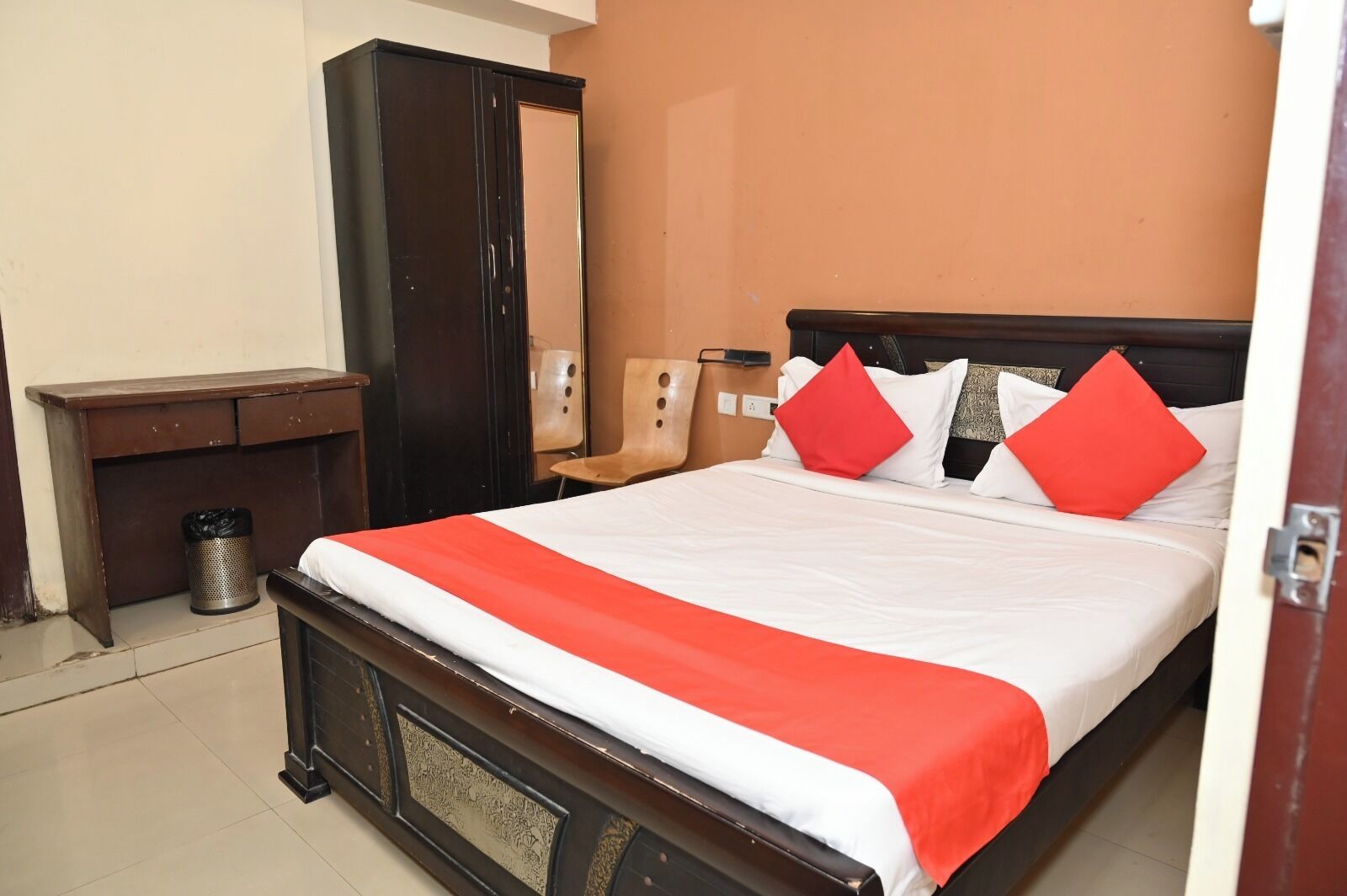 Quarto de hotel com uma cama, uma escrivaninha de madeira, um cesto de lixo e um guarda-roupa.