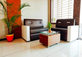 Uma área de espera moderna com um sofá de couro preto, uma mesa de centro com tampo de vidro e uma planta em vaso vermelho.