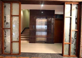 Interior com elevador central, escadaria e painéis de vidro decorativos com motivos florais.