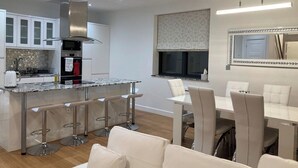 Cozinha moderna com ilha central, banquetas e área de jantar com cadeiras brancas.