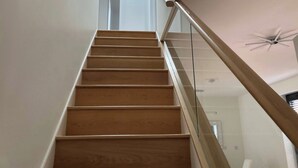 Uma escada de madeira com guarda-corpo de vidro que dá para um patamar.