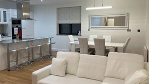 Uma cozinha moderna com uma ilha central, banquetas de bar e uma área de jantar com mesa e cadeiras brancas.