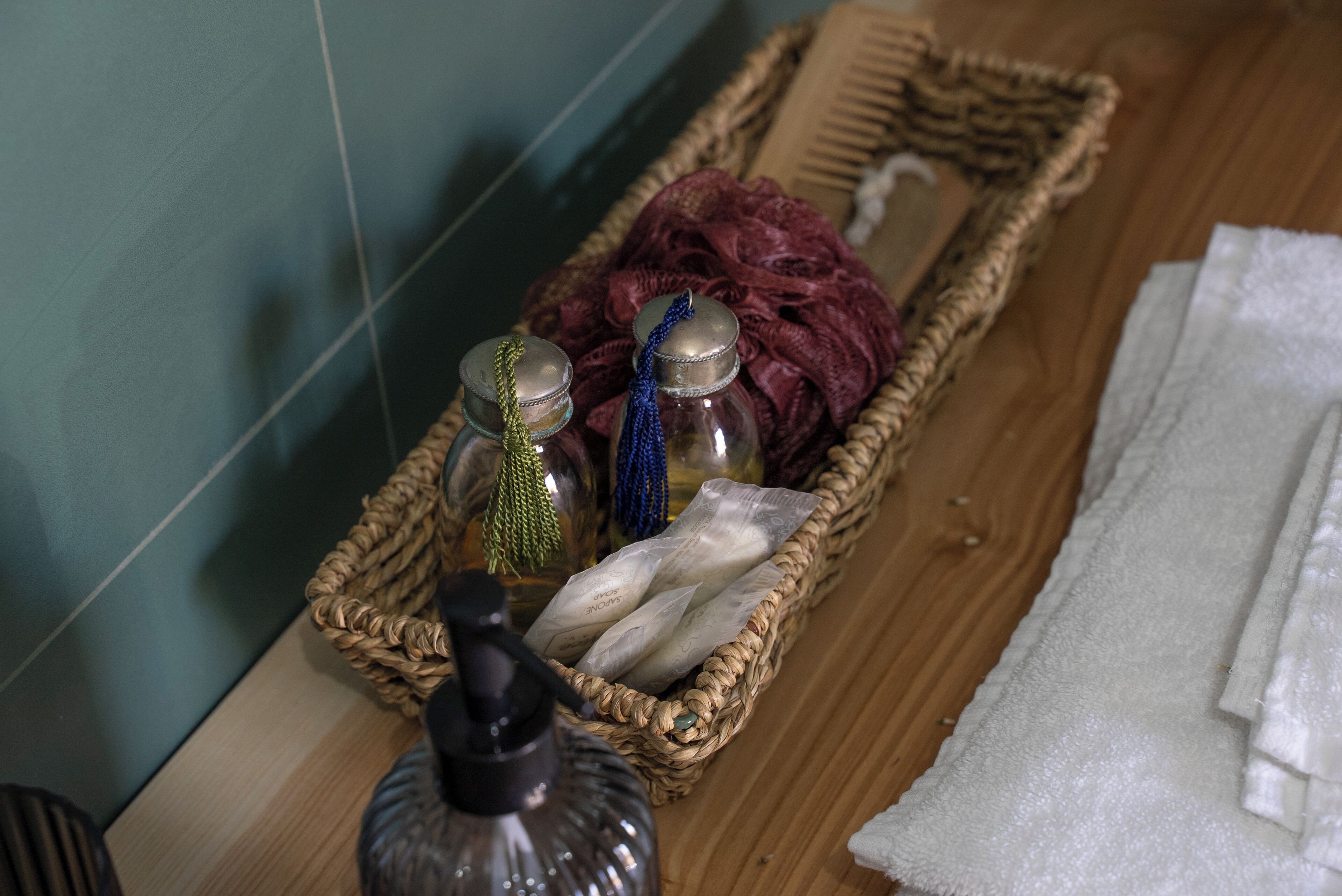 Uma cesta de vime com produtos de higiene pessoal, uma garrafa e um tecido vermelho sobre uma superfície de madeira.