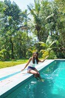 Uma pessoa sentada na borda de uma piscina, rodeada por vegetação exuberante.
