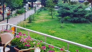 Varanda com cadeiras e plantas em vasos, com vista para uma área gramada com árvores e um caminho.