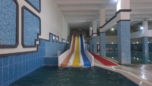 Piscina interior em vários níveis, com um escorregador colorido, paredes azulejadas e área de água cristalina.