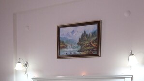 Cama bem arrumada com lençóis brancos e toalha em formato de cisne, pétalas de rosa vermelhas espalhadas sobre a cama, e uma pintura de uma paisagem montanhosa acima da cama.