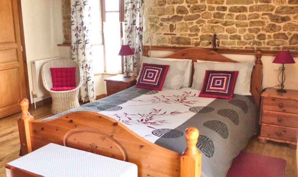 Uma cama de madeira com colcha estampada, uma cadeira de vime e uma mesa de cabeceira de madeira com abajur.