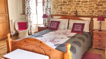 Uma cama de madeira com colcha estampada, uma cadeira de vime e uma mesa de cabeceira de madeira com abajur.