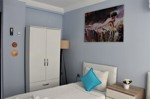 Quarto com cama, mesa de cabeceira, luminária, quadro e armário.