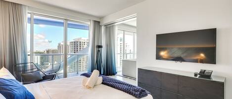 Quarto de hotel moderno com uma cama grande, uma escrivaninha, uma cadeira, uma televisão e uma varanda com vista para a cidade.