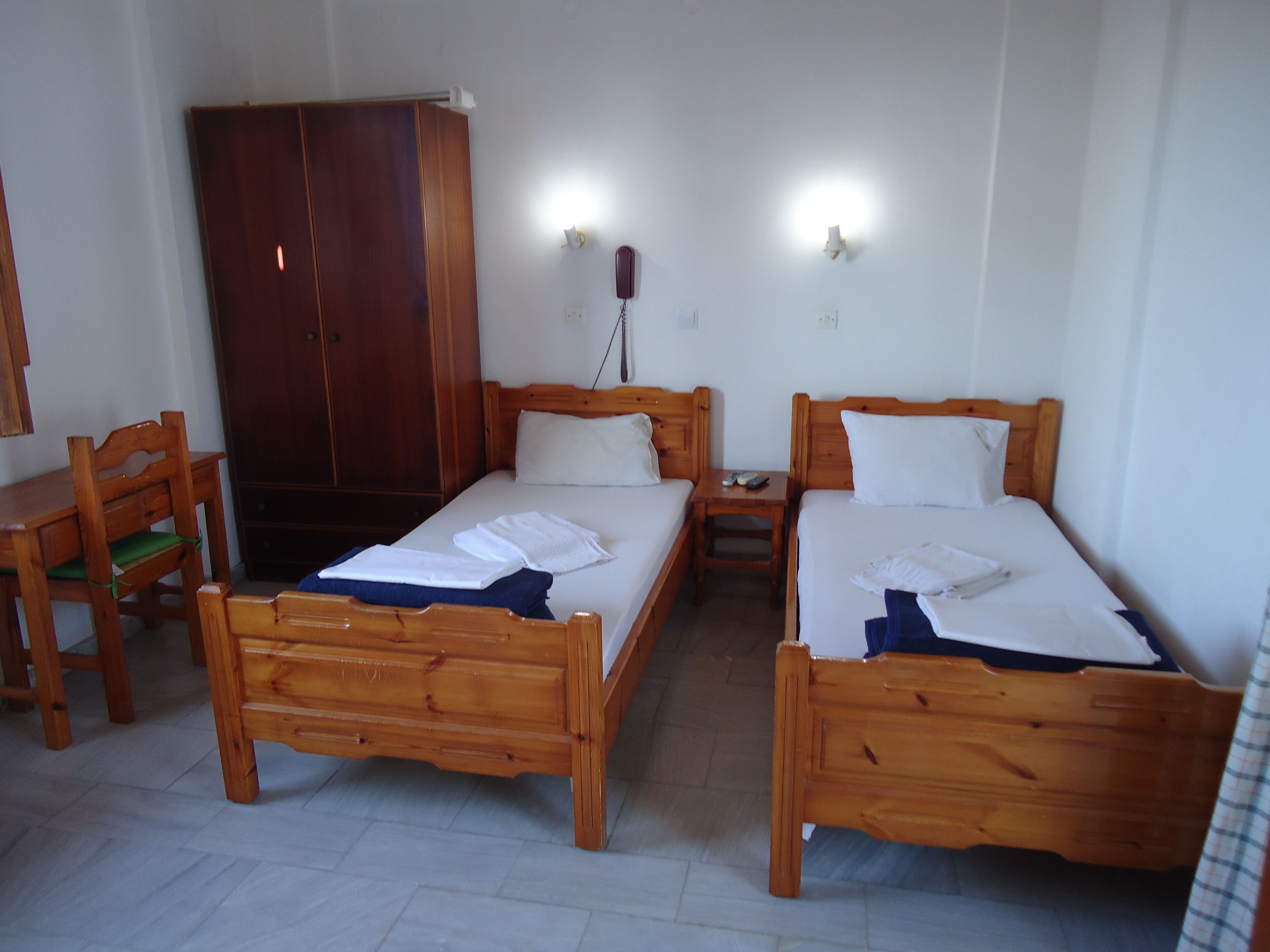 Quarto com duas camas de madeira, um guarda-roupa de madeira, uma escrivaninha de madeira e uma cadeira.