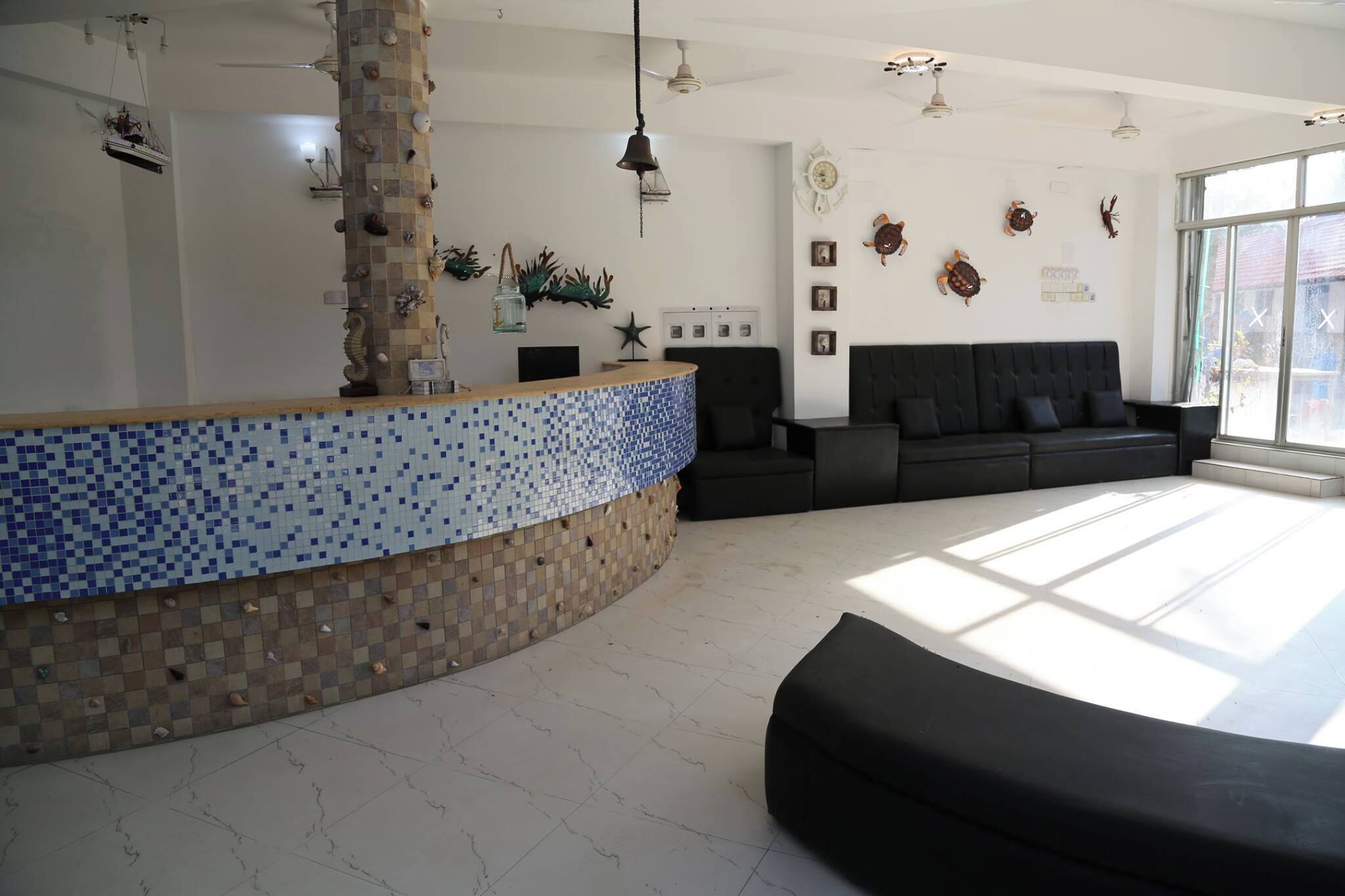 Uma área de recepção com balcão revestido em mosaico, sofá preto e uma grande janela que oferece luz natural.