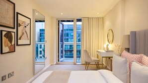 Quarto de hotel moderno com uma cama grande, uma escrivaninha, uma cadeira e vista para a cidade pela janela.