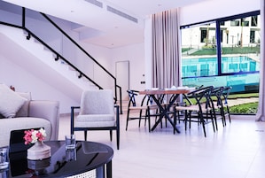 Uma sala de estar moderna com escada, área de jantar com vista para a piscina e sofá com almofadas decorativas.