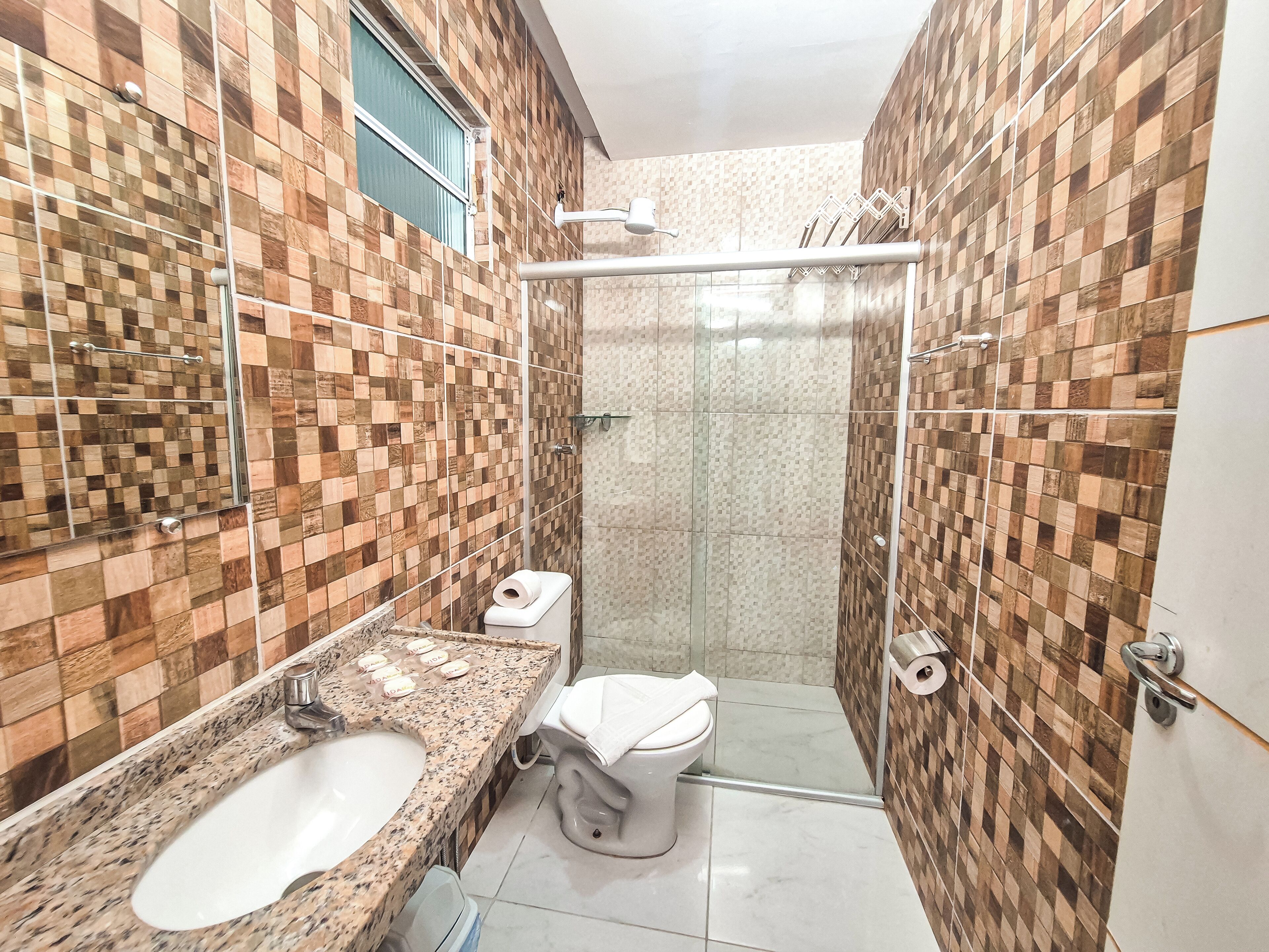 Um banheiro com parede de azulejos quadriculados, pia, vaso sanitário e área de chuveiro.