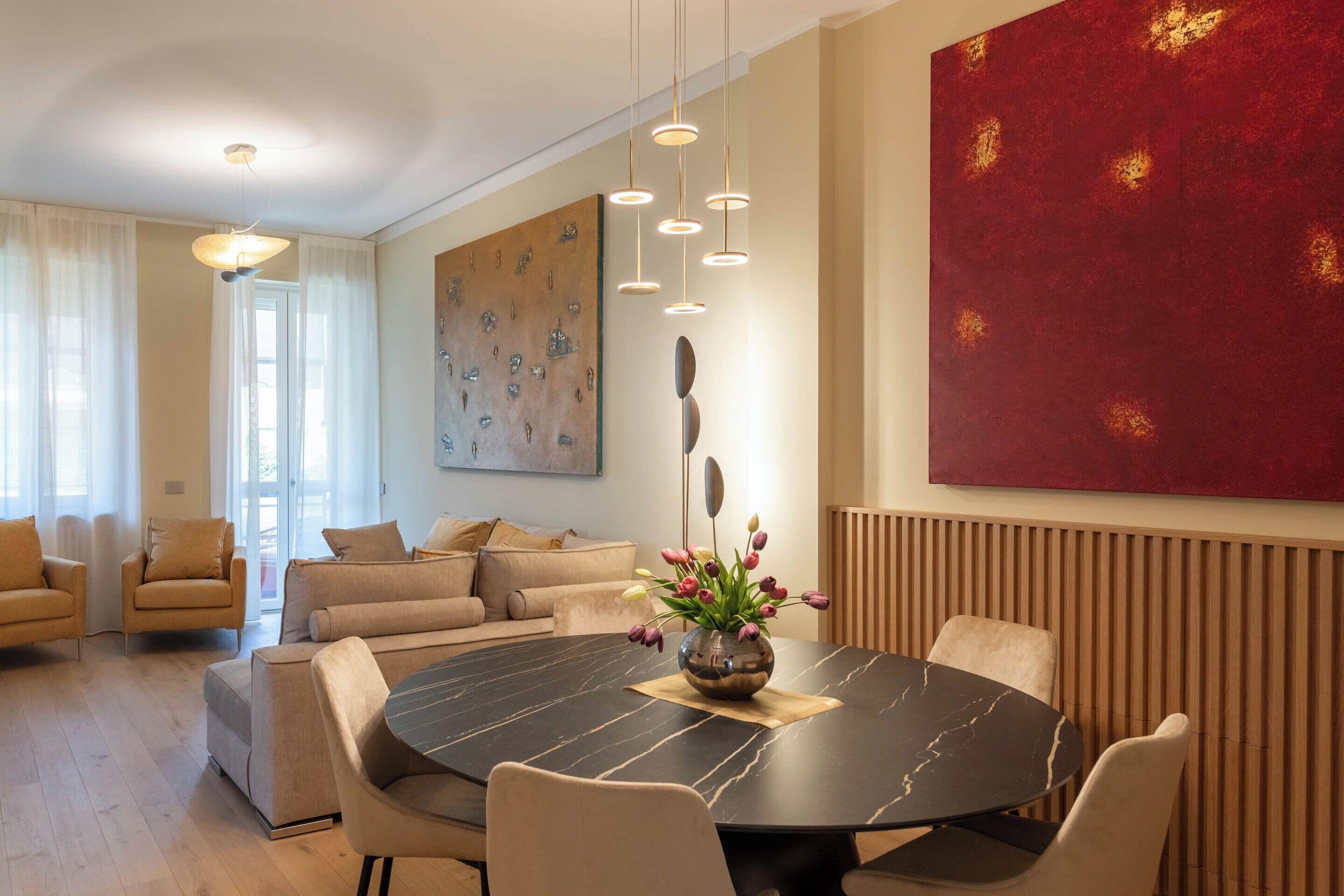 Uma sala de estar moderna com uma mesa de jantar redonda, sofás bege e um quadro abstrato grande.