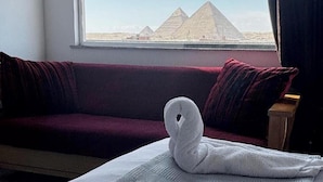 Quarto com vista para as pirâmides, um sofá vermelho e uma toalha branca em formato de cisne na cama.