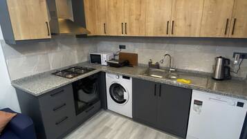 Uma cozinha compacta com armários de madeira, máquina de lavar embutida, lava-louças e fogão a gás.