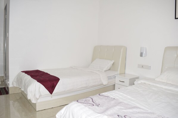 Quarto de hotel com duas camas, uma mesinha de cabeceira e uma luminária fixada na parede.