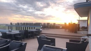 Área externa com mesas e cadeiras, com vista para o horizonte urbano ao pôr do sol.