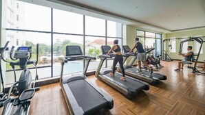 Uma academia com esteiras, bicicletas ergométricas e uma grande janela com vista para edifícios e áreas verdes.
