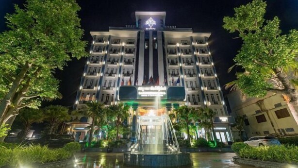 Um hotel com vários andares, com uma fonte central, rodeado por vegetação exuberante e iluminado por iluminação artificial.