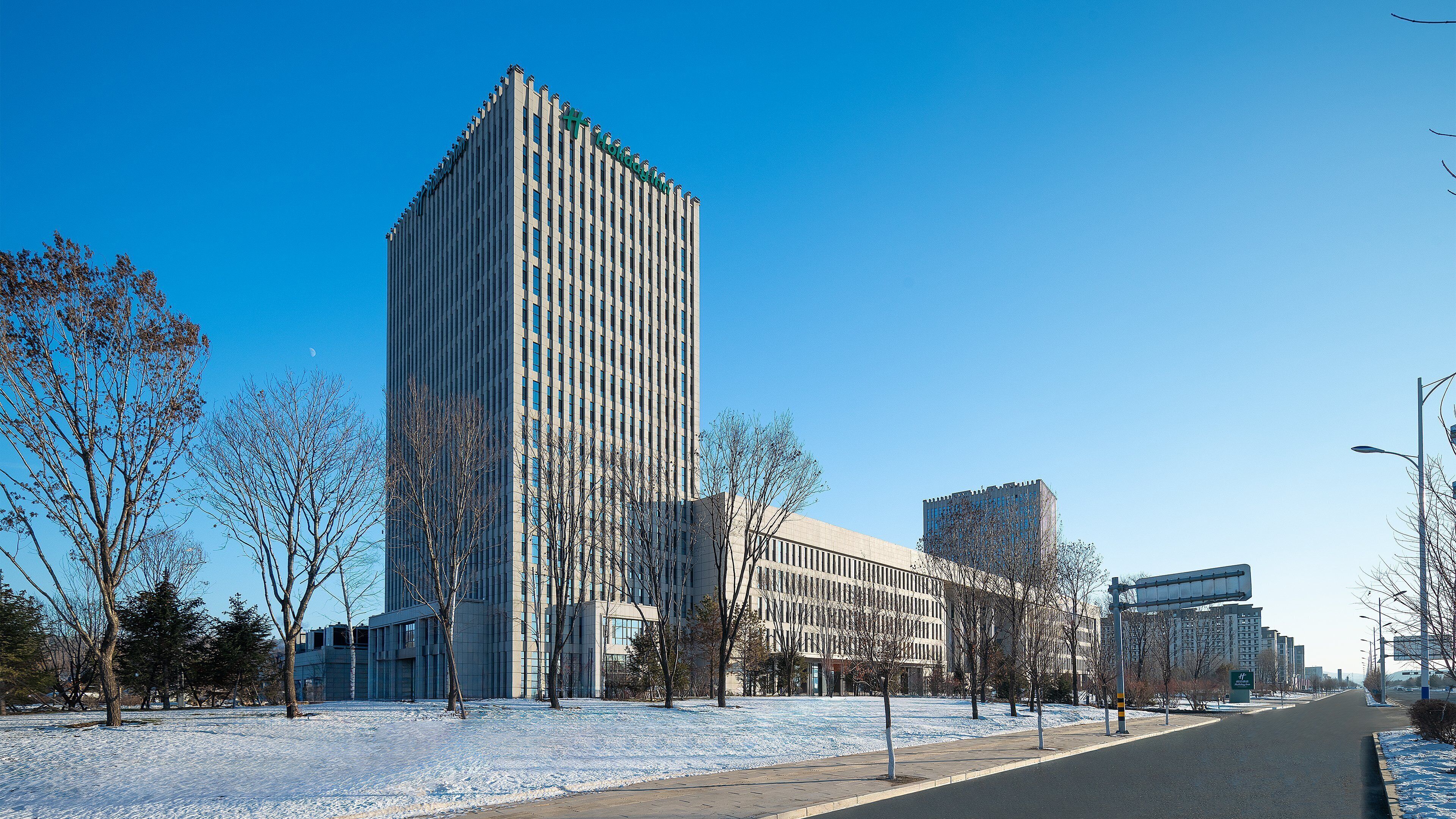 Um edifício alto com design moderno, rodeado por terreno coberto de neve e árvores sem folhas.