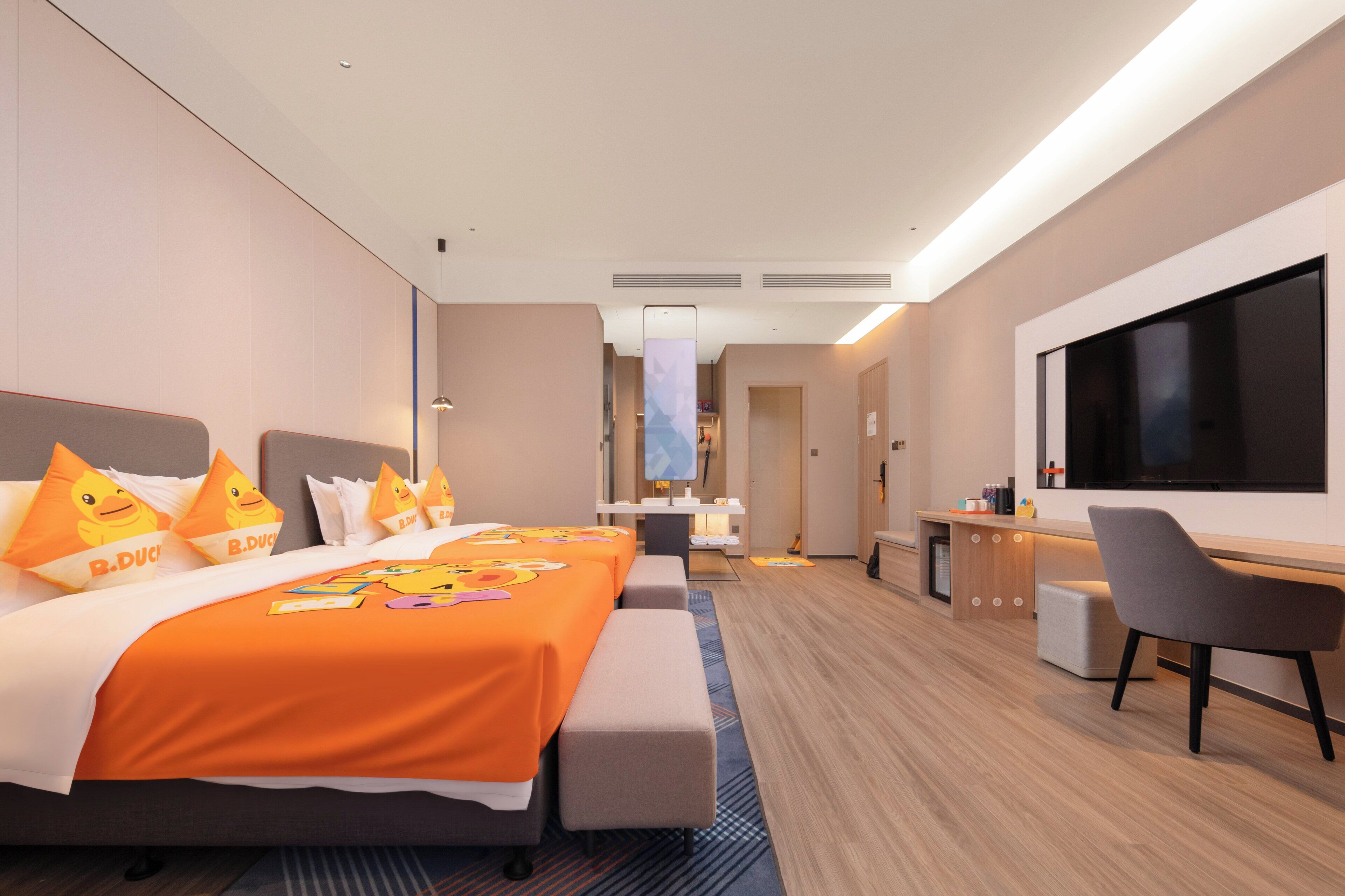 Quarto de hotel com cama grande, escrivaninha, televisão e banheiro ao fundo.